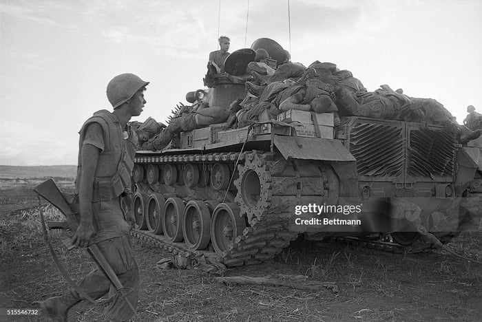 A U. S. tank carrying the bodies of fallen Marines moves out, following ...
