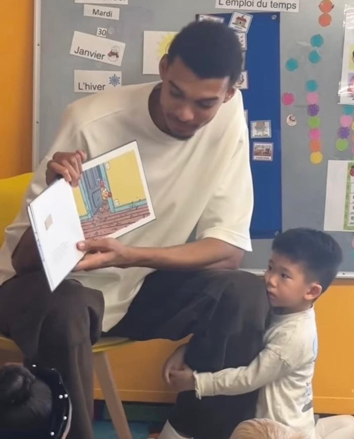 Little kid hugs Victor Wembanyama's leg as he's reading a book to the ...