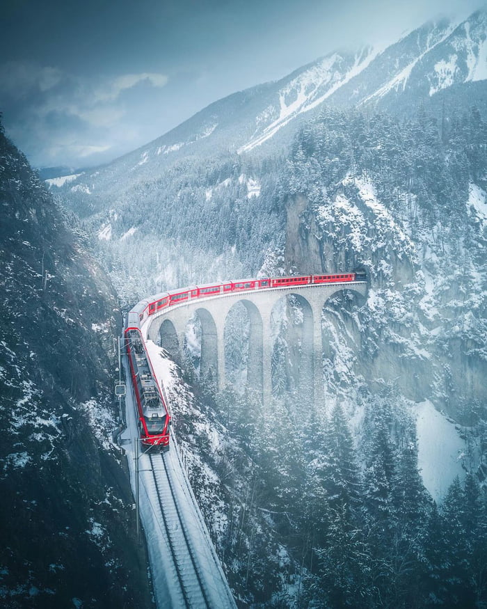 A bright red train snakes through the snow-capped Alps mountain range ...