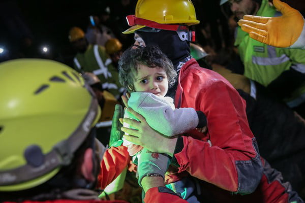 Search-and-rescue personnel hold a young child pulled from the rubble ...